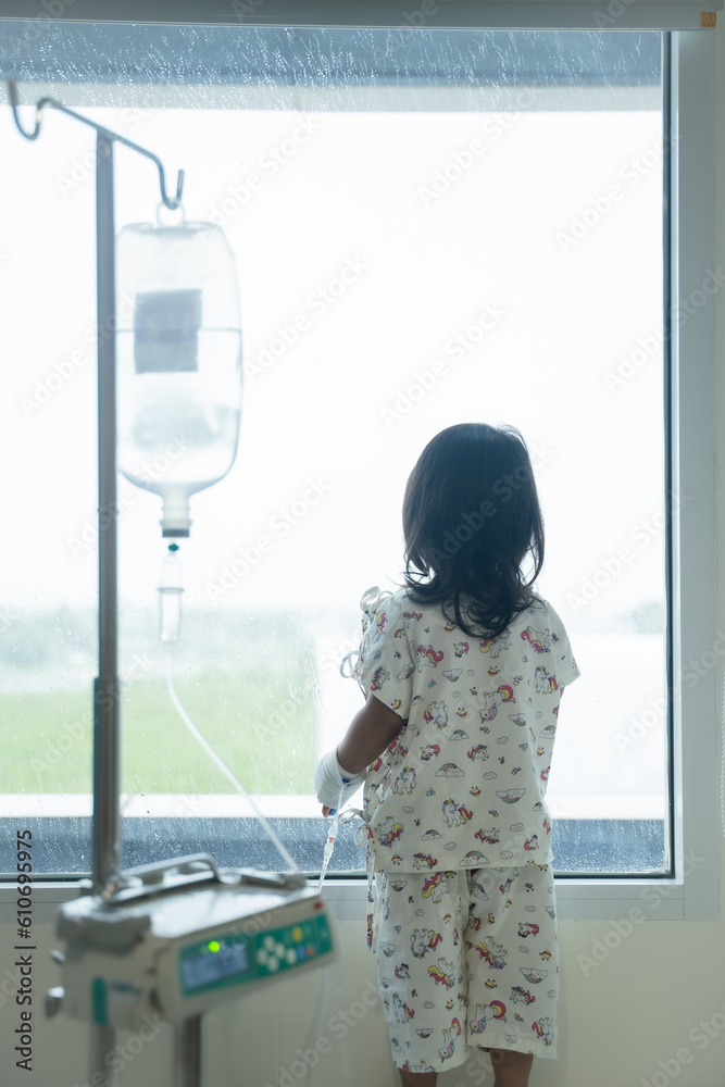 Child wearing IV tube is standing and looking out the window in ...