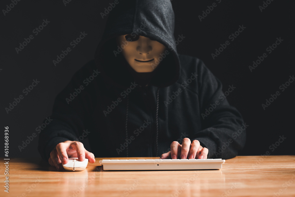 Black hat hacker in hood using tablet on desk to hacking privacy sensitive data cyber crime hack ...