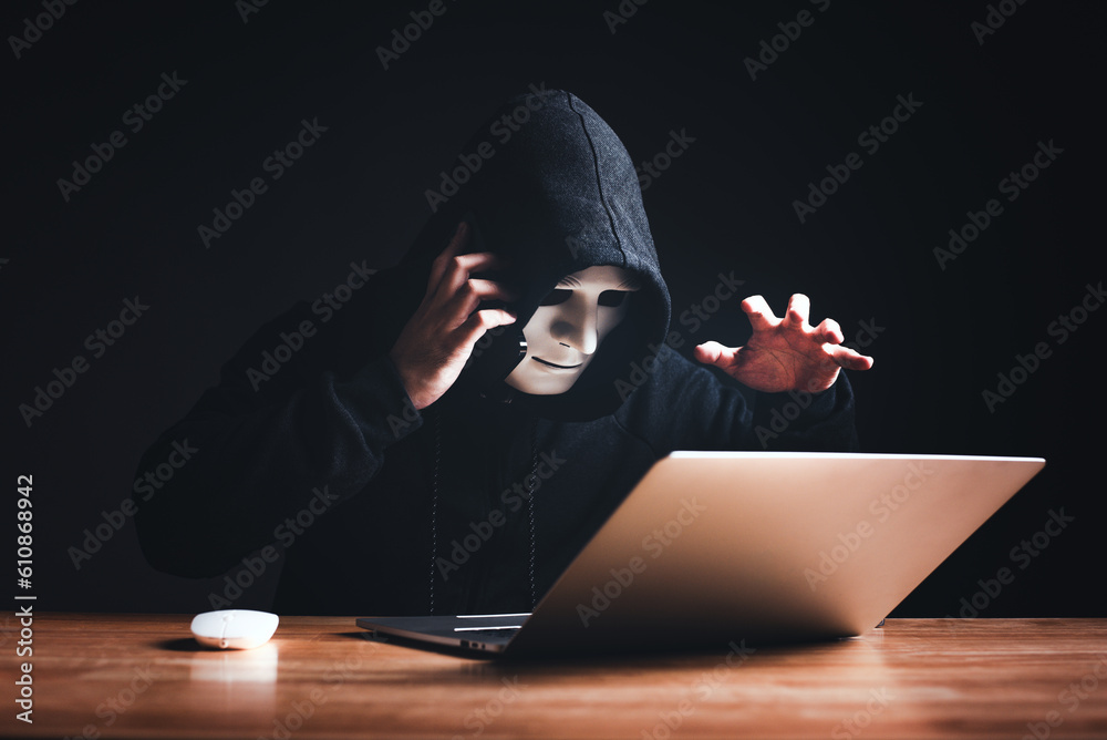 Black hat hacker in hood using laptop computer and call smartphone to ...