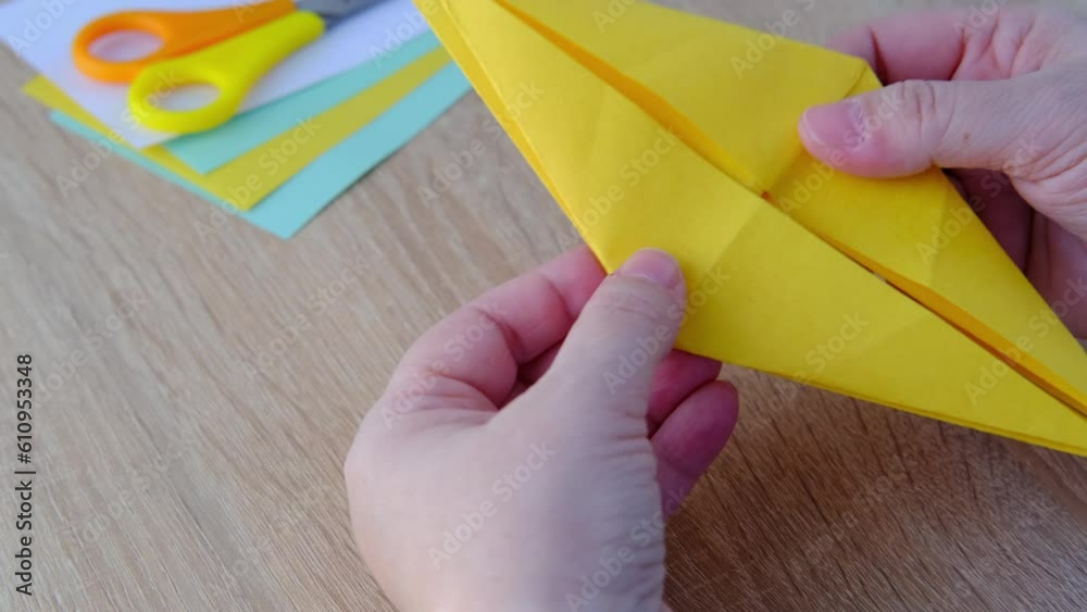 close-up of colored paper, female hands fold Japanese crane figurine in ...