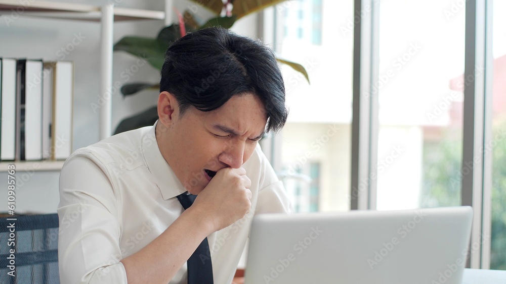 Exhausted young asian worker yawning at workplace. Business man using ...