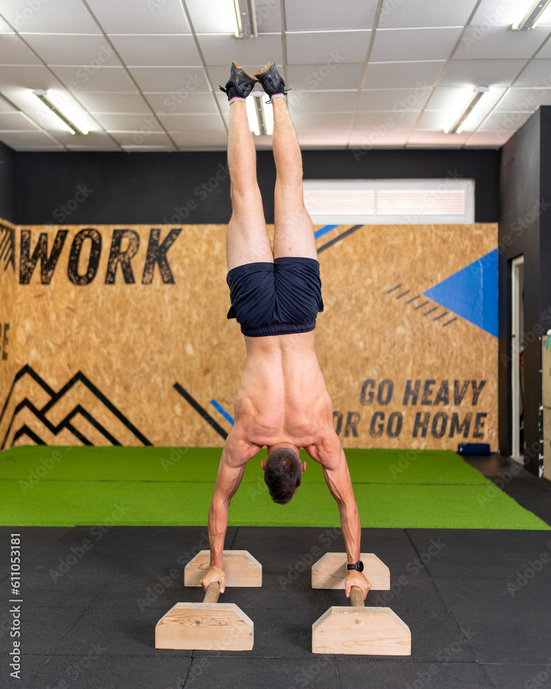 Shirtless young man performing a handstand on bars during training at ...