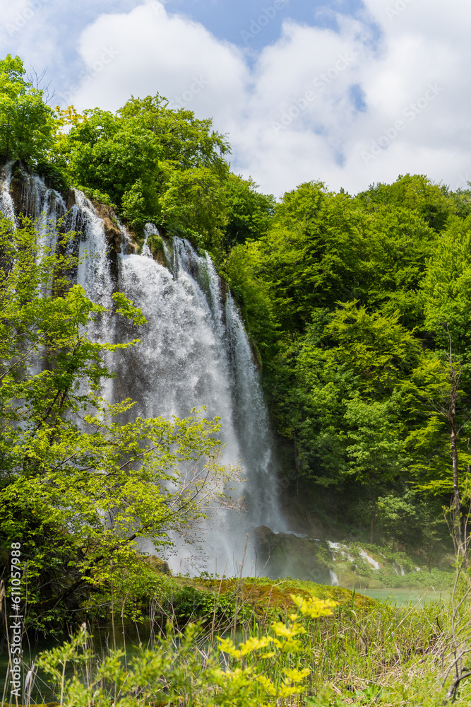 Großer Wasserfall im Nationalpark Plitvicer Seen an Felswand vor einem See mit vielen Pflanzen ...