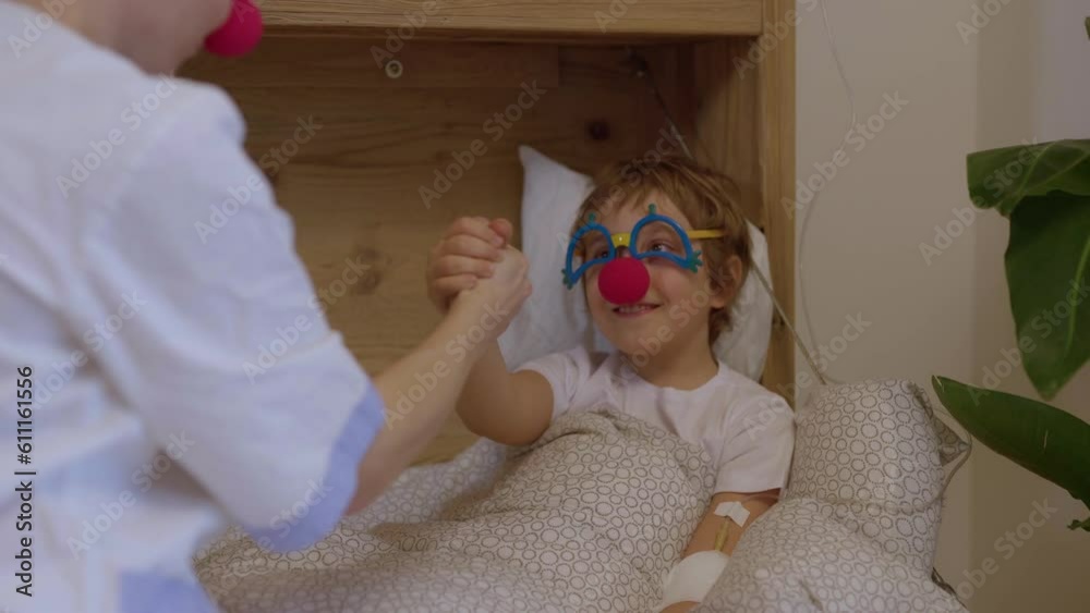 Medical sister with a red nose plays with a boy in his hospital ward ...