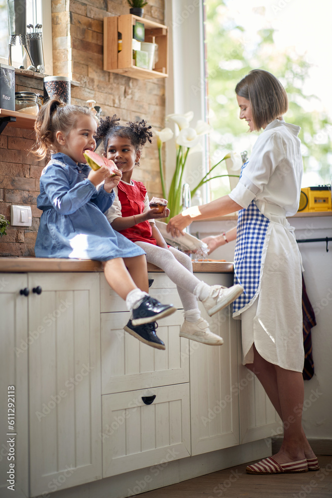Two cute little girls sitting on countertop eating a snack, watermelon ...