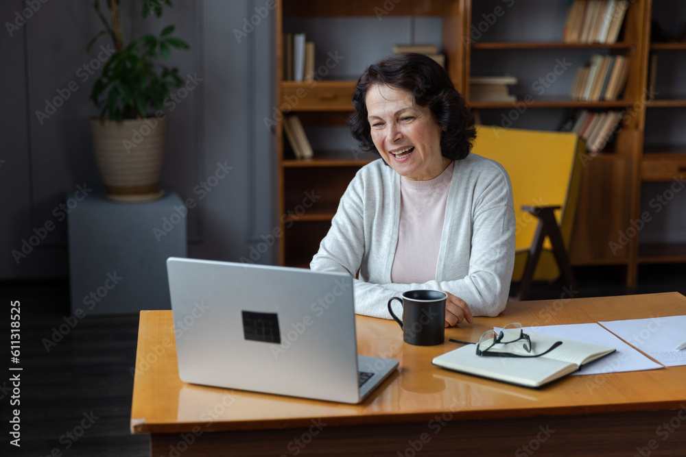 Fototapeta: Happy middle aged senior woman sit with laptop talk on ... Fototapeta: Happy middle aged senior woman sit with laptop talk on ...