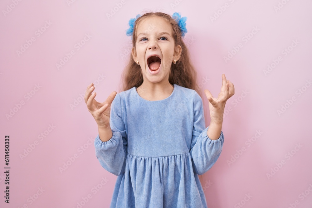 Young little girl standing over pink background crazy and mad shouting ...