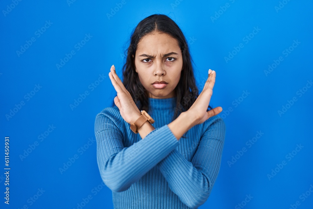 Young brazilian woman standing over blue isolated background rejection ...