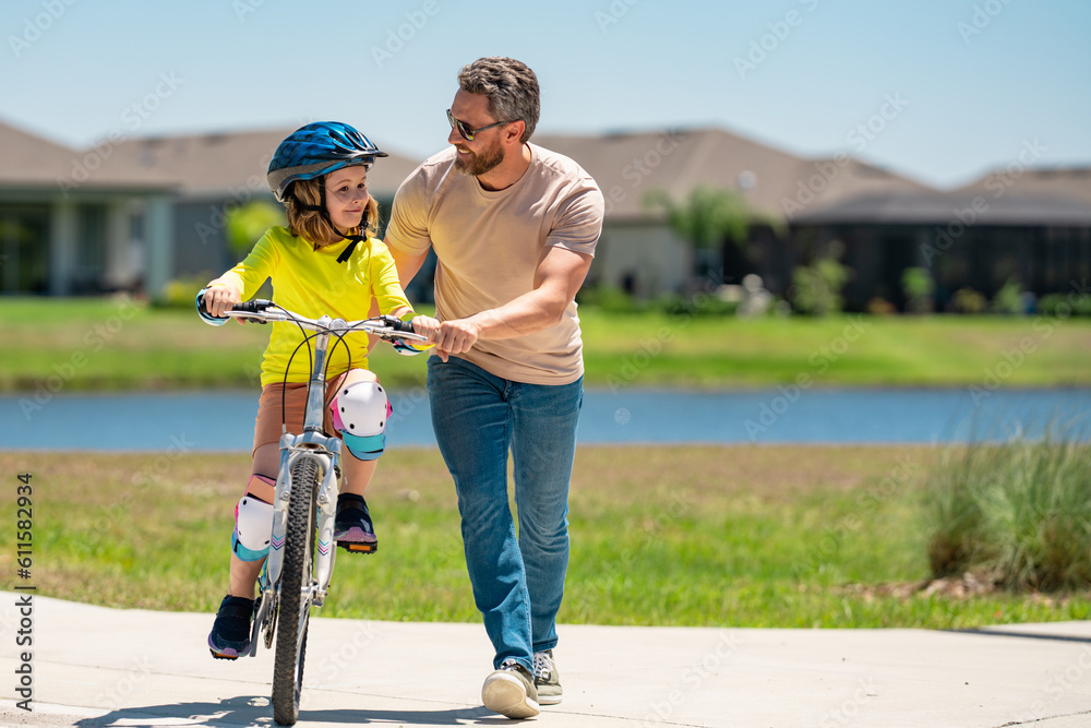 Fathers day. Boy learning to ride a bicycle with his father in park. Father teaching his son ...