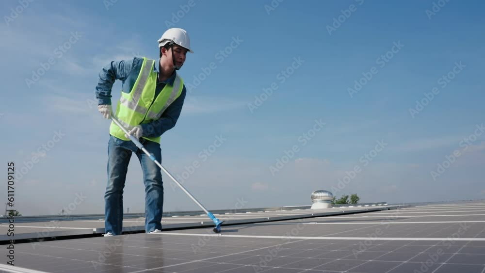 Asian handyman man using mop cleaning glass solar panel on rooftop ...
