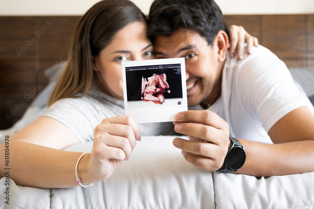 happy married couple look at the camera showing an ultra sound image of ...