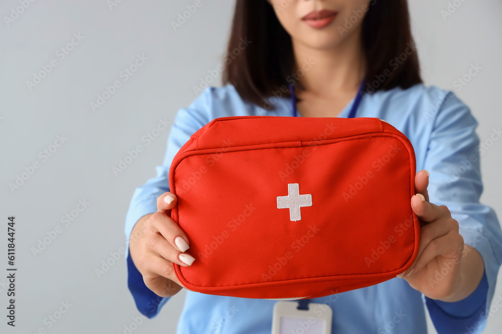 Female Asian medical intern with first aid kit on grey background ...