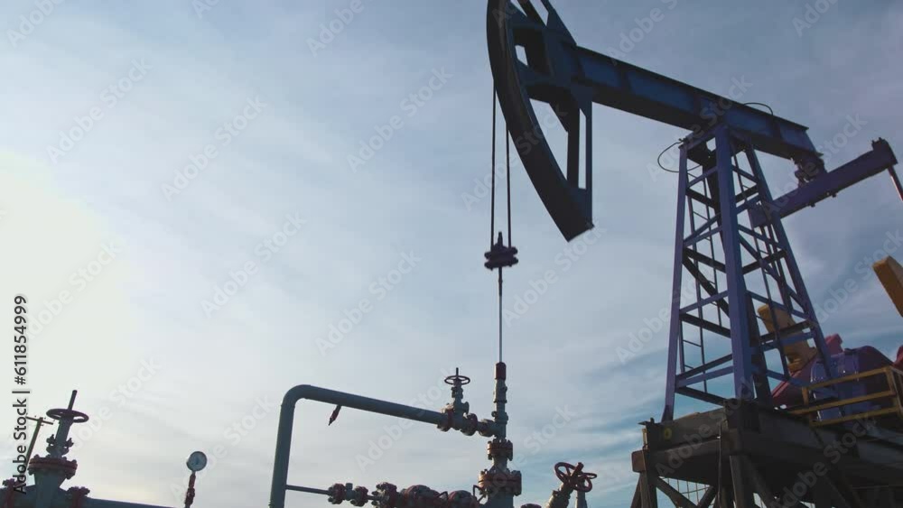 Low angle shot of working oil pump rig at sunny day against blue sky ...