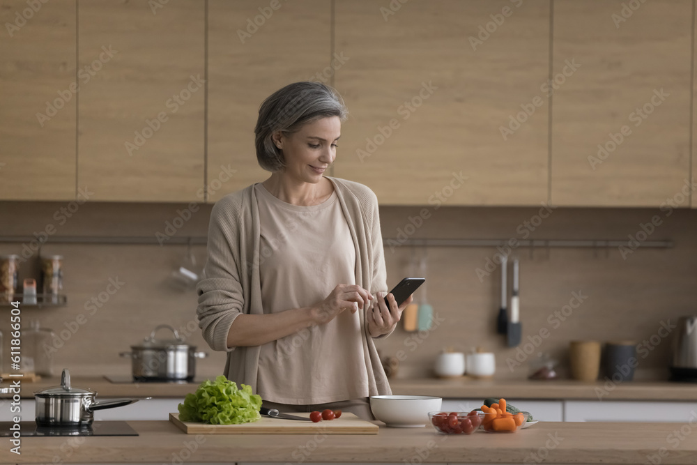 Positive mature chef blogger woman using smartphone over table with ...