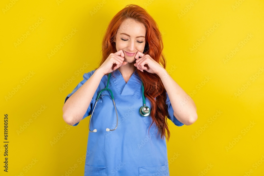 Pleased young red-haired doctor woman over yellow studio background ...