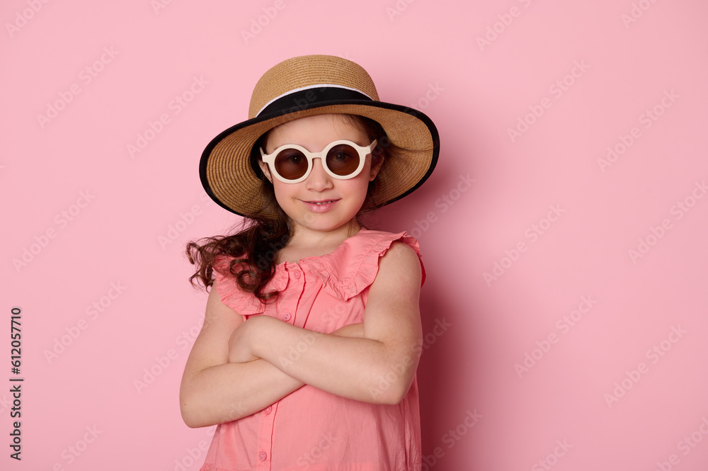 Mischievous kid girl in sunglasses, pink dress and straw hat, smiling ...