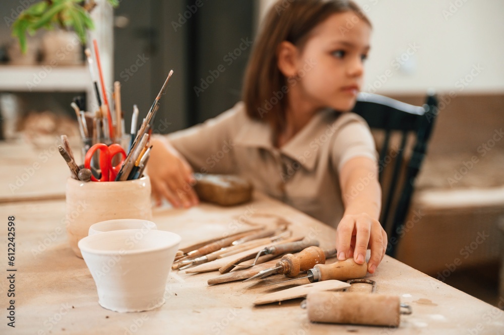 Different tools on the table. Little girl is learning how to do pottery ...