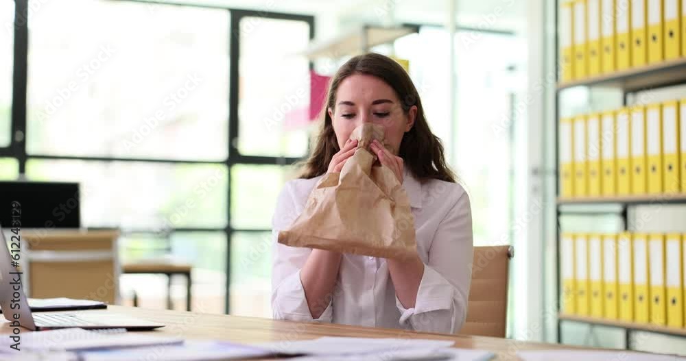 Frightened woman breathing into paper bag at workplace. Panic attack at ...