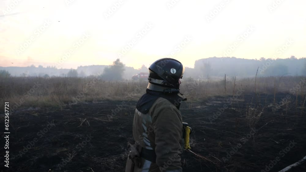 Young fireman in uniform going on burnt grass at countryside. Male ...