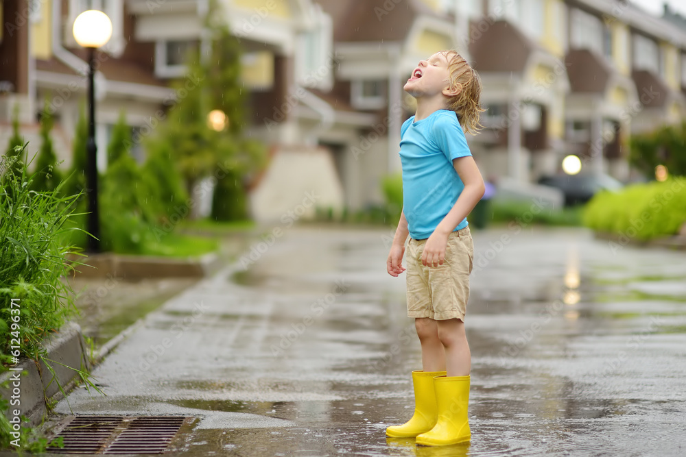Little boy wearing yellow rubber boots walking on rainy summer day in ...