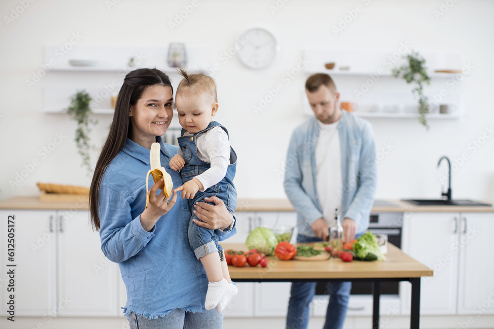 Cheerful caucasian mother proposing baby tasty banana while father ...