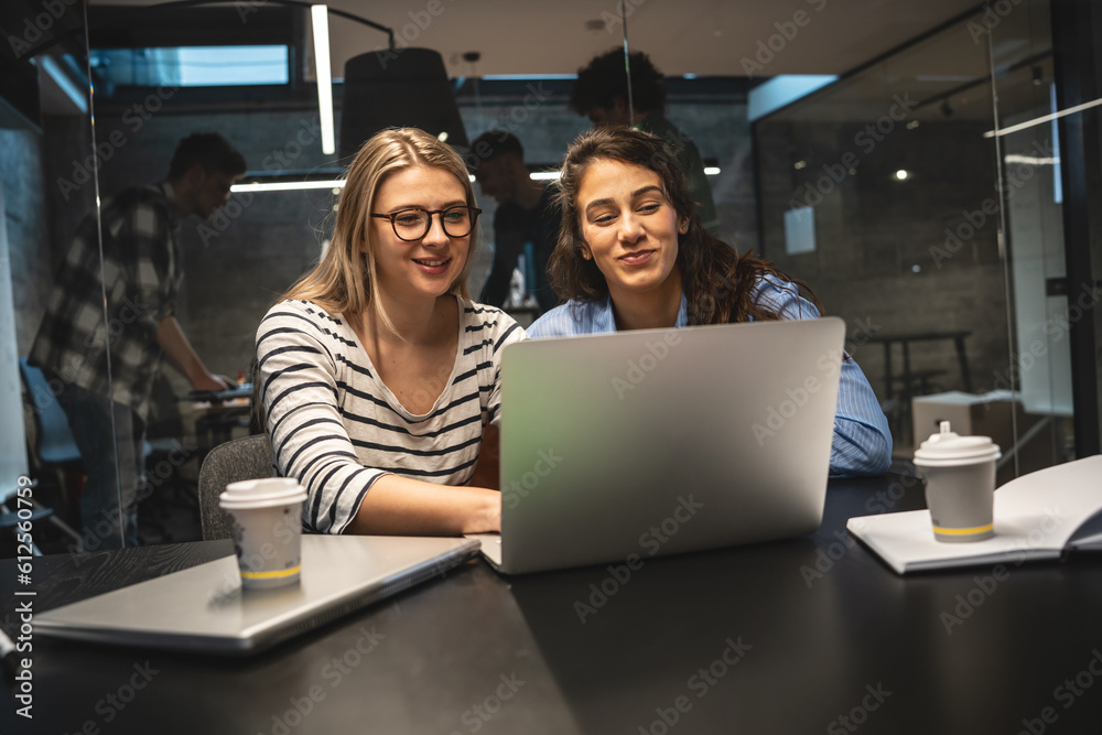 Two female programmers and engineers work alongside their colleagues in an office, collaborating ...