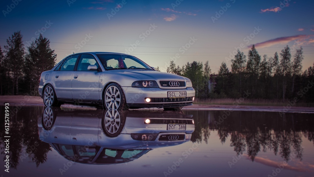 Audi A4 B5 and its reflection on a wet road at sunset as seen from the ...