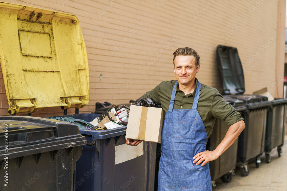 Garbage sorting with blond smiling man wearing blue apron. Man holds ...