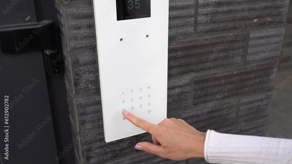 Caucasian woman dials an apartment code on an electronic doorphone ...