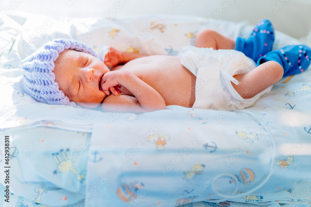 Portrait of cute premature baby boy dressed in a blue knitted wool cap ...