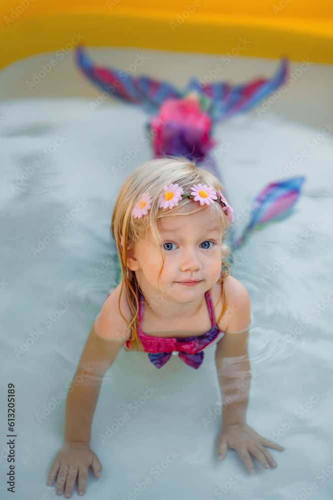 Little blonde toddler girl with mermaid bathing suit in splashing water ...