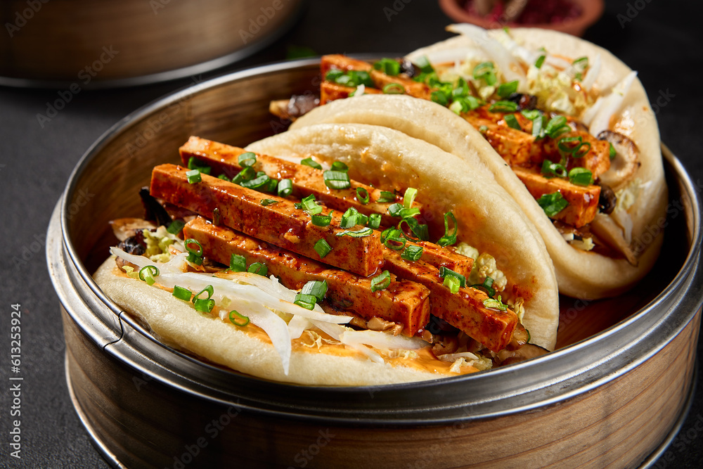 Side view of bao buns with tofu and vegetables in a steamer on a black ...