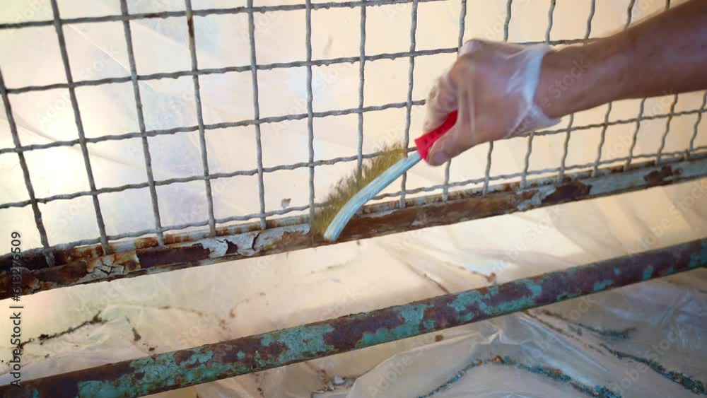 Workman grinding metal gate surface with handheld brush removing old ...