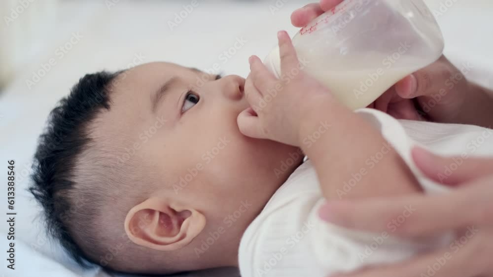 Adorable little Asian baby drinking from baby bottle. Asian Mother take care adorable her son ...