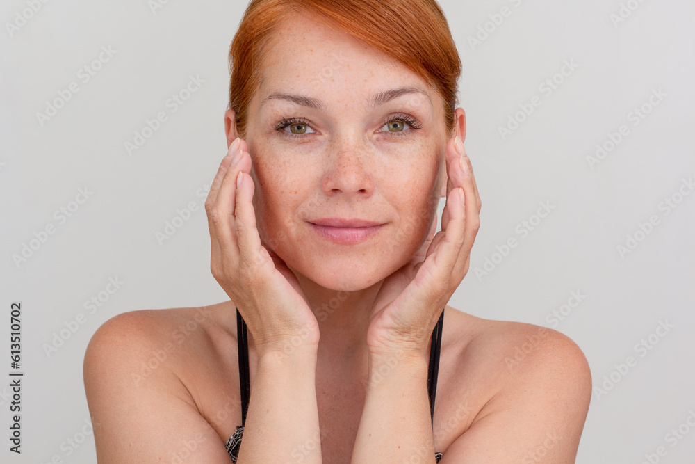 Portrait of cropped caucasian middle aged woman face with freckles touching skin by hands on ...