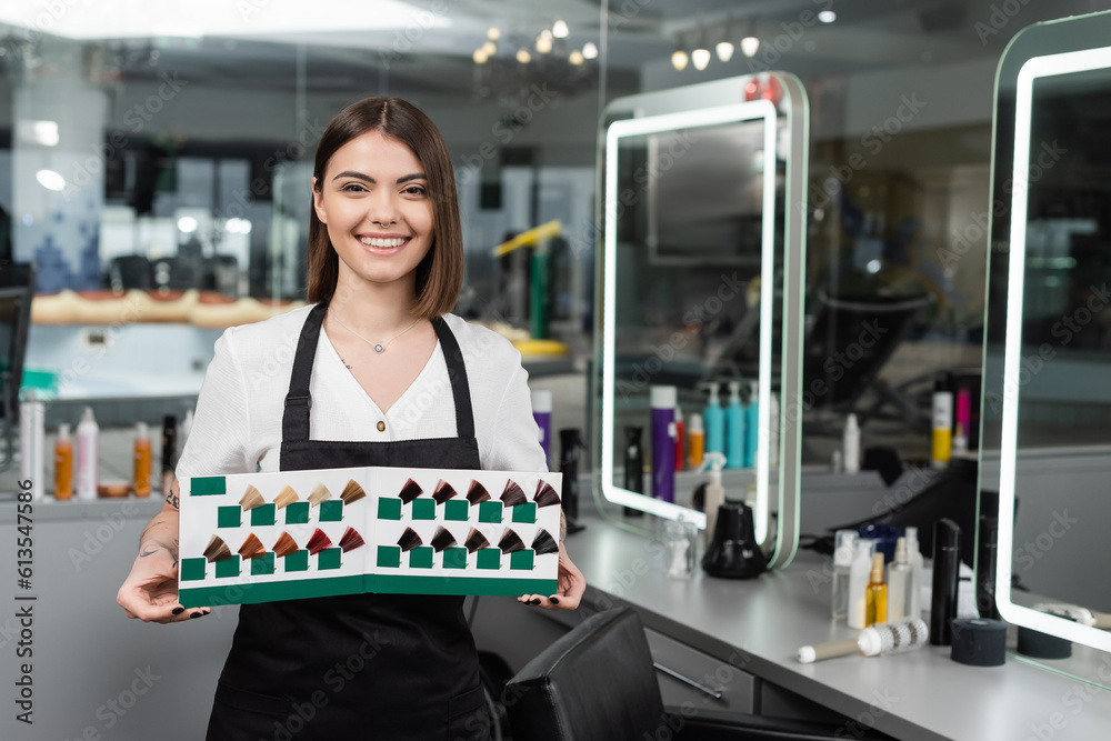 hair salon, happy beauty worker in apron showing hair color palette in ...