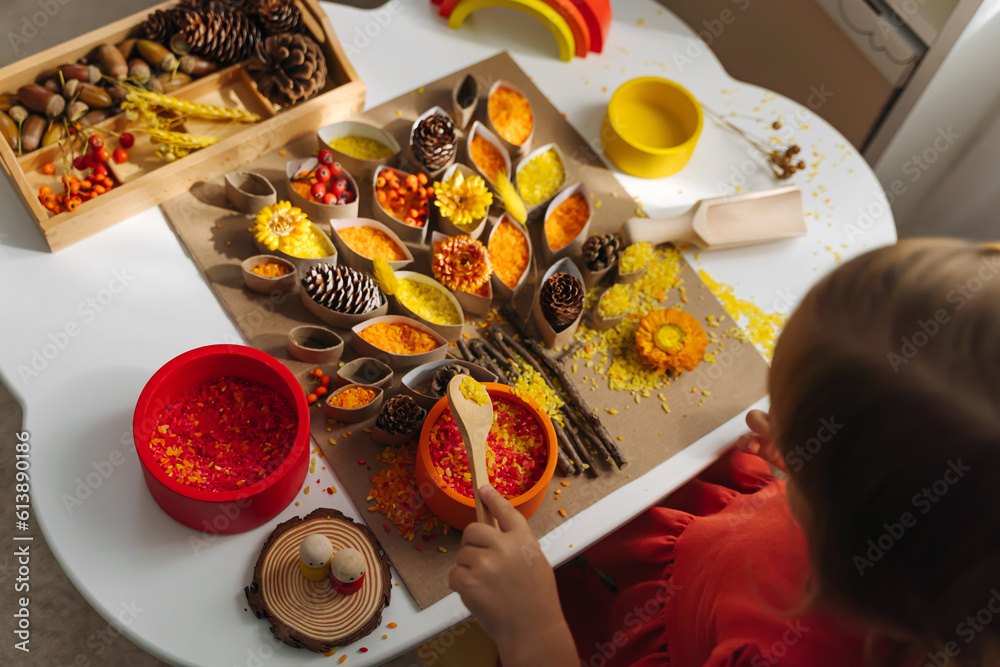 A little girl playing with autumn natural materials and make a tree ...