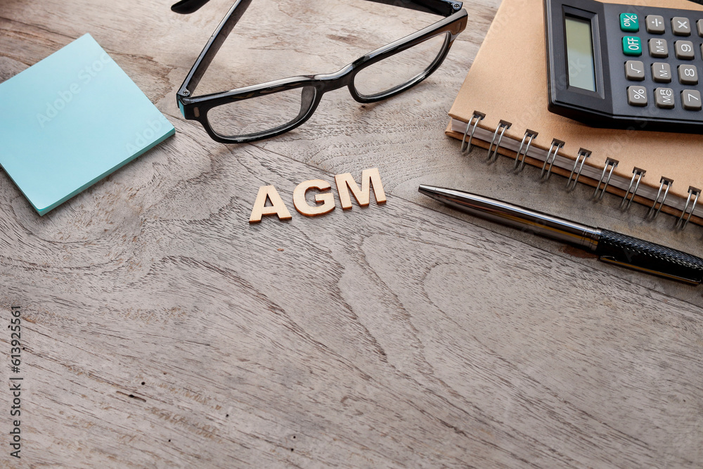 The word AGM is made from wood on the wooden table with a post-it note ...