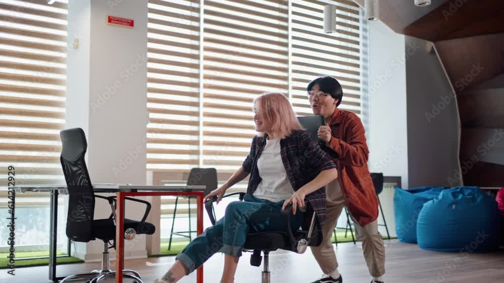 Young Asian student pushing his classmate in an office chair down the ...