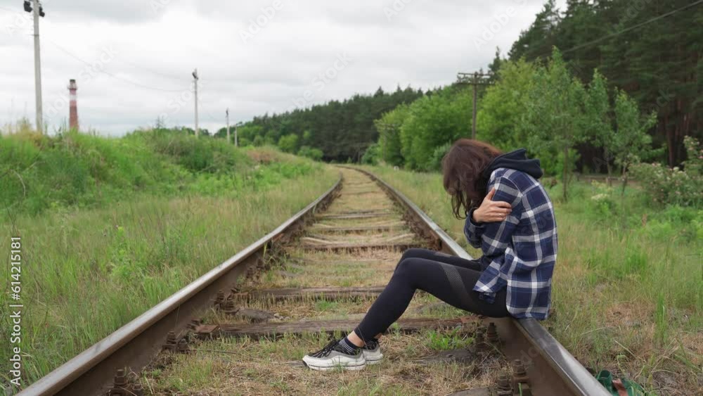 A lonely young woman sits on the rails with her arms around herself and ...