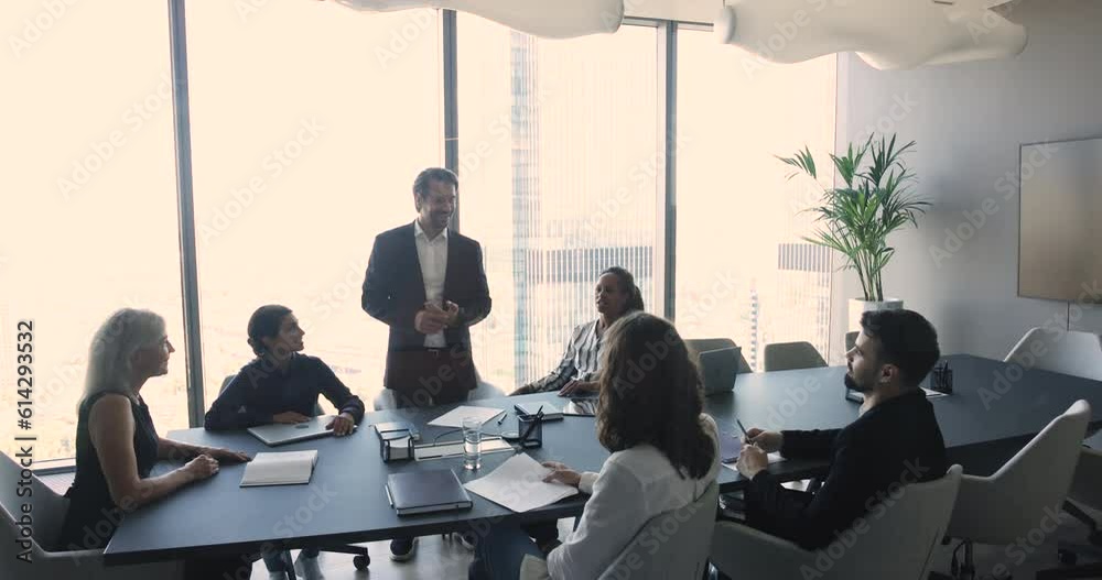 Positive handsome male boss talking to diverse team, standing at ...
