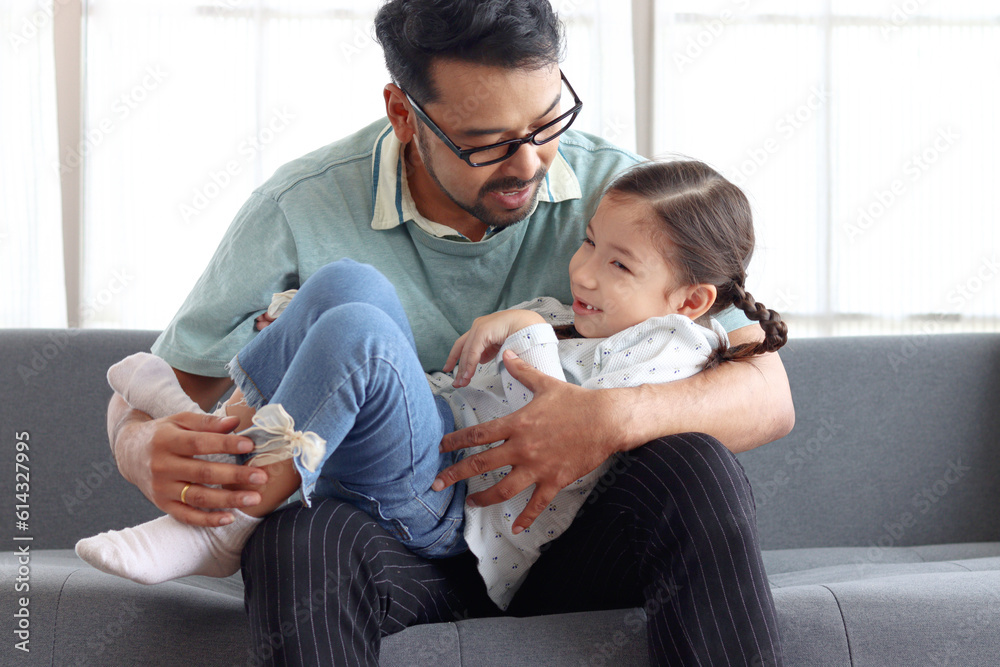 Cute little girl sits on daddy lap on sofa in living room, playing and ...