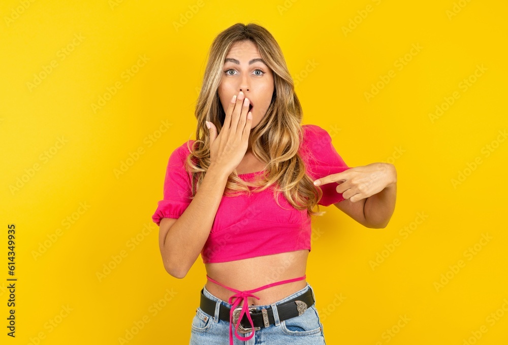 Shocked young blonde woman wearing pink crop top over yellow studio ...