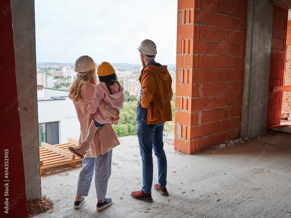Back view of parents with daughter standing inside apartment building ...