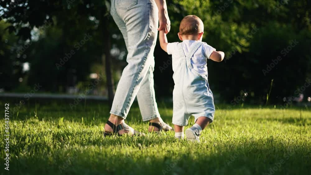Happy family. Baby takes first steps with his mother in park on grass ...