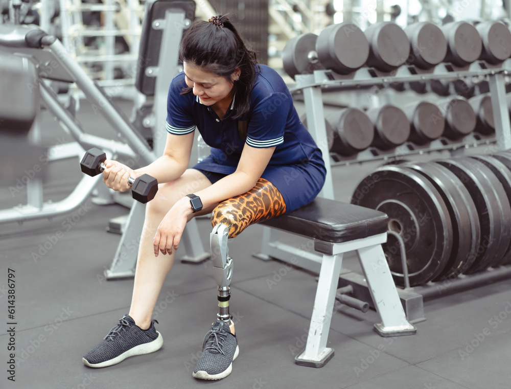 Woman with prosthetic leg sitting in gym lifting dumbbell weight. Asian ...