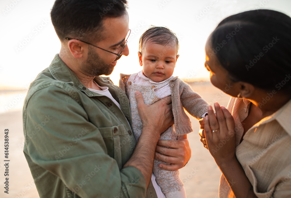 Loving young parents enjoying family tender moments with little infant son outside, walking on ...