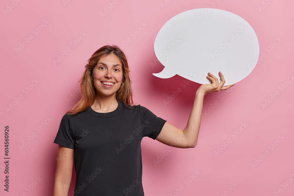 Cheerful Young European Woman Beams With Wide Smile While Holding Speech Bubble Overhead Eagerly