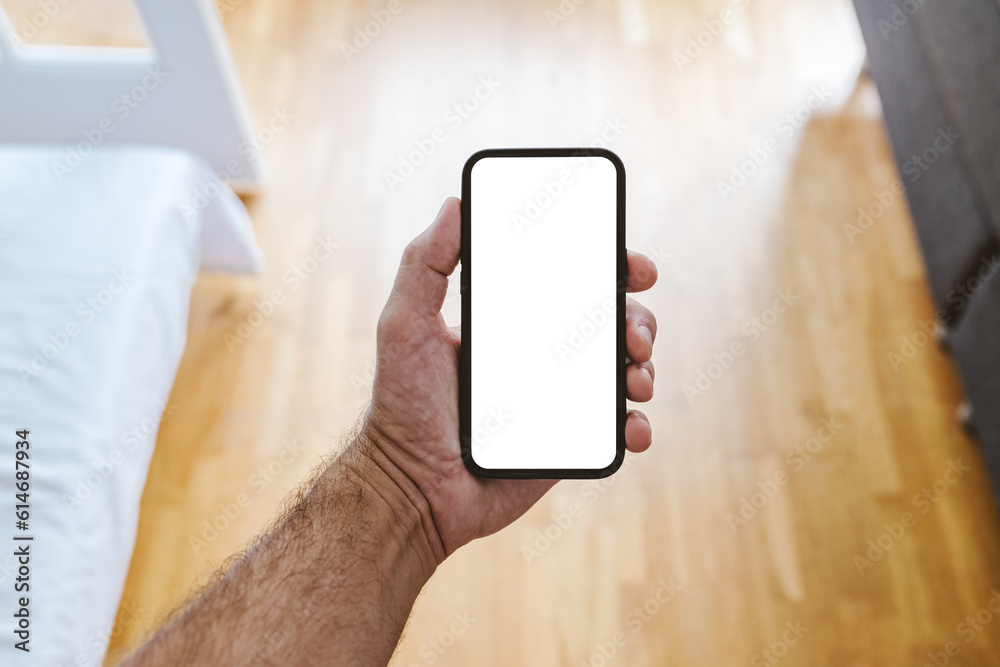 Man holding smart phone device with blank mockup screen in bedroom. Copy space for app or text ...