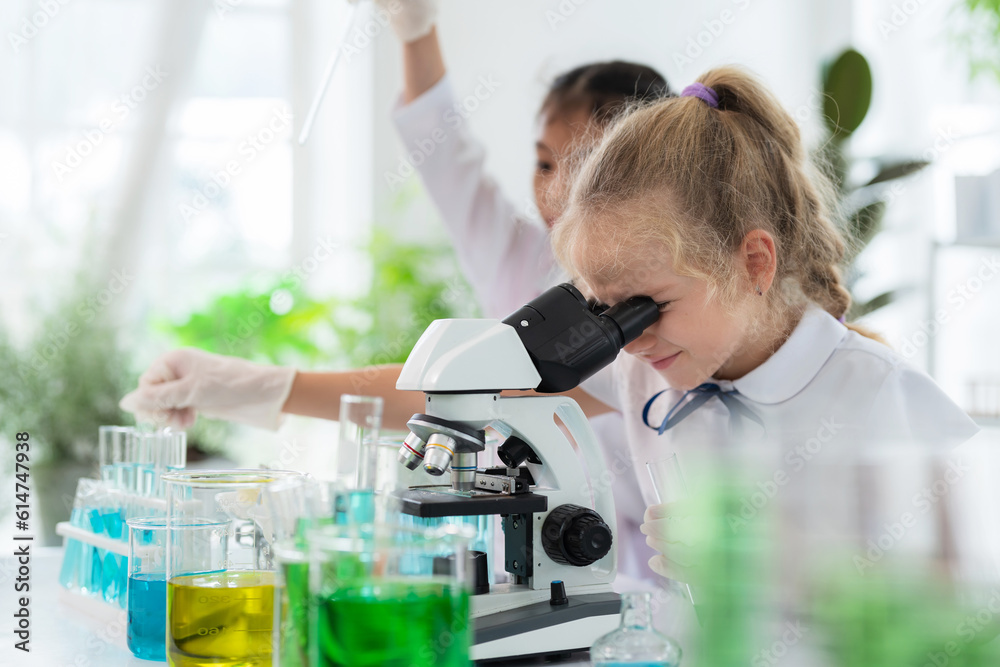 Young Caucasian scientist girl wearing lab coat and using microscope to see the structure of ...